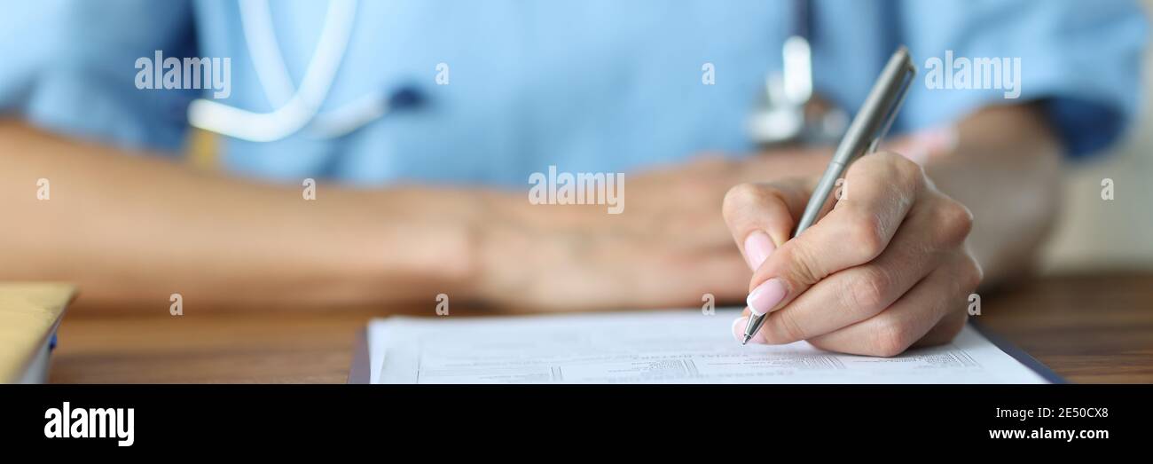 Doctor writing with ballpoint pen in document at table in clinic close ...