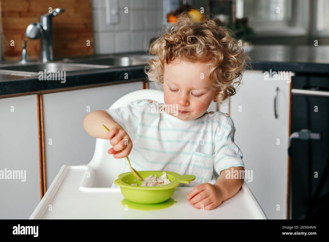 Cute adorable Caucasian curly kid boy sitting in chair eating cereal ...