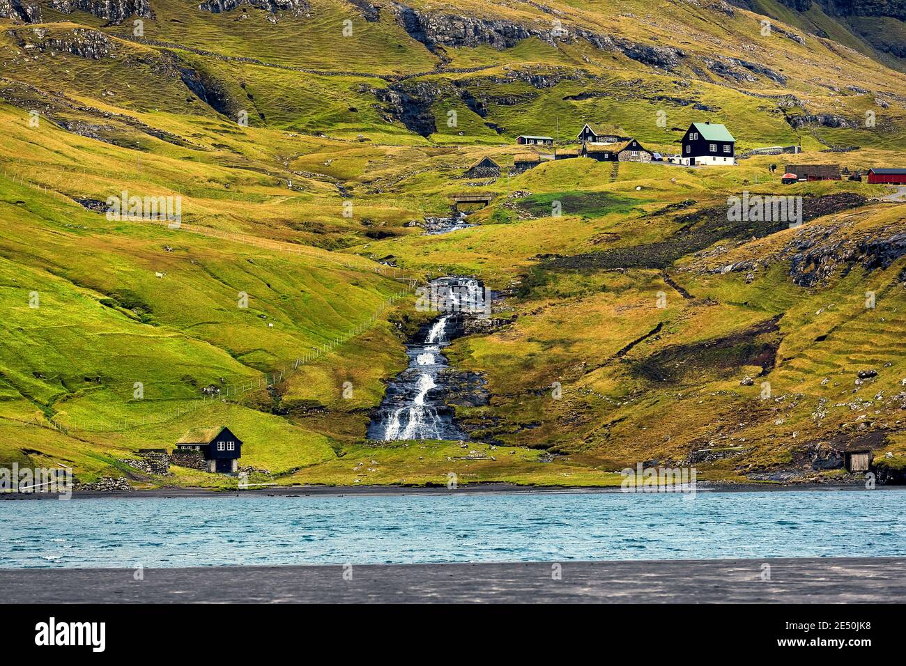 Small waterfall and small houses in green valley. Coastline of Atlantic ...