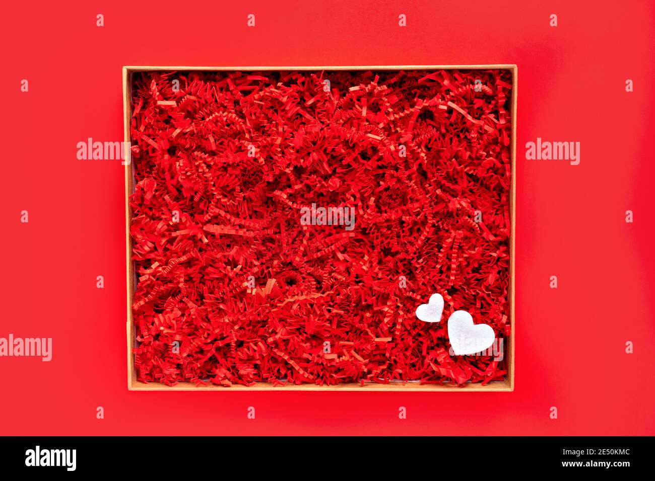 Opened gift box with shredded red paper on plain red background. Flat ...