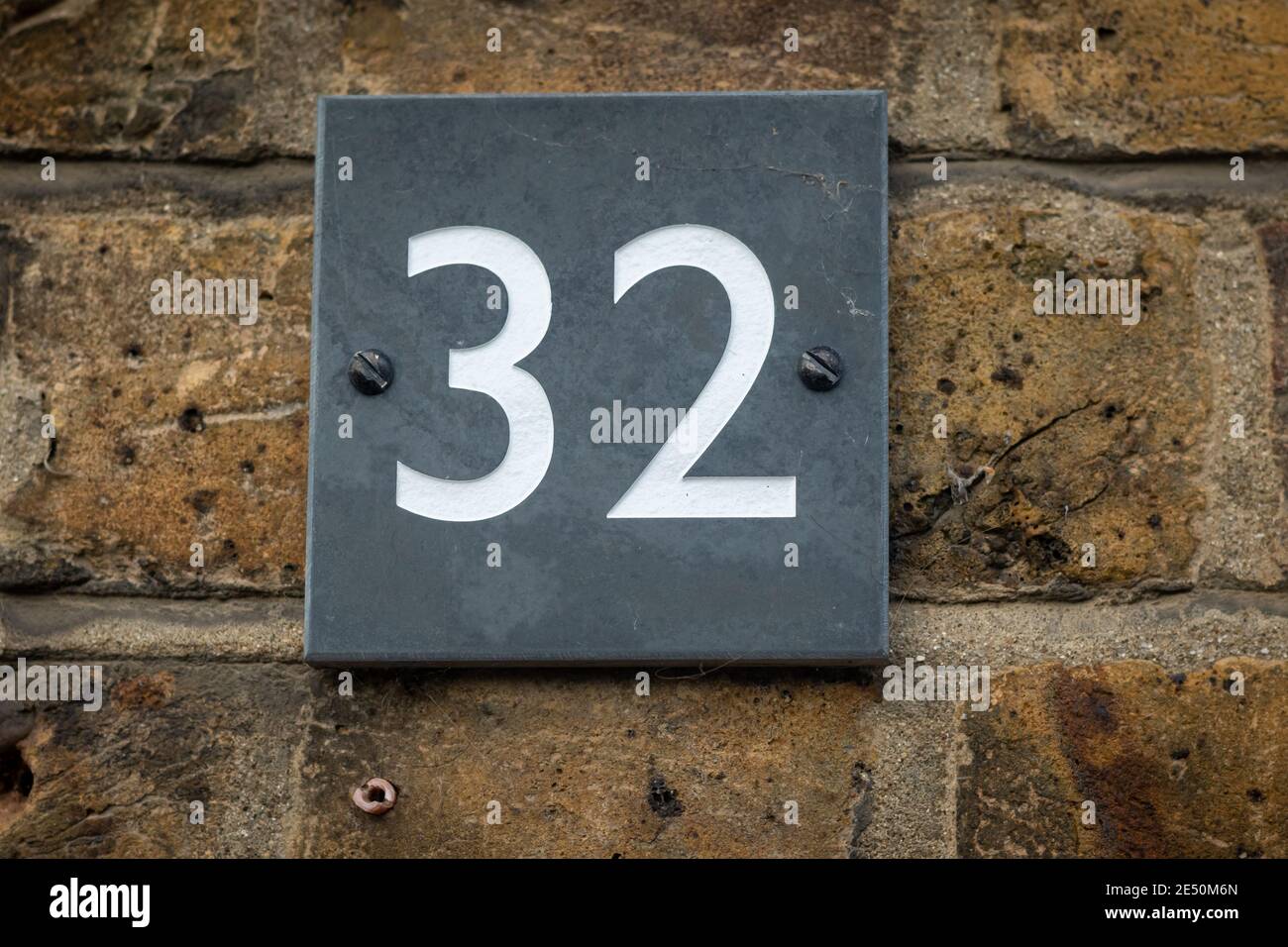 Number 32 carved into a granite plaque on a yellow brick wall Stock ...