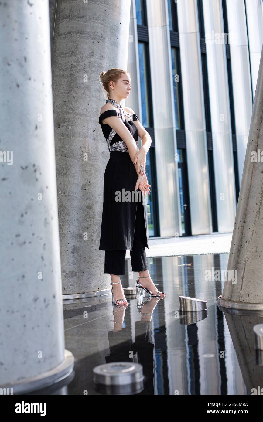 Young white model girl standing on the floor among concrete columns ...