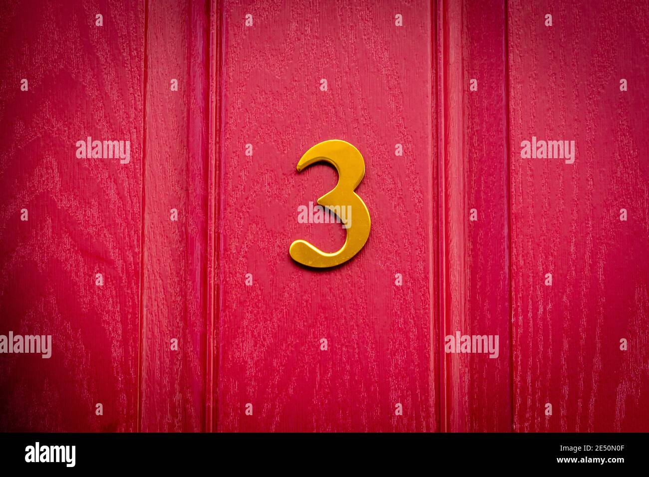 Golden number 3 on a red woodne front door with dark corners Stock ...