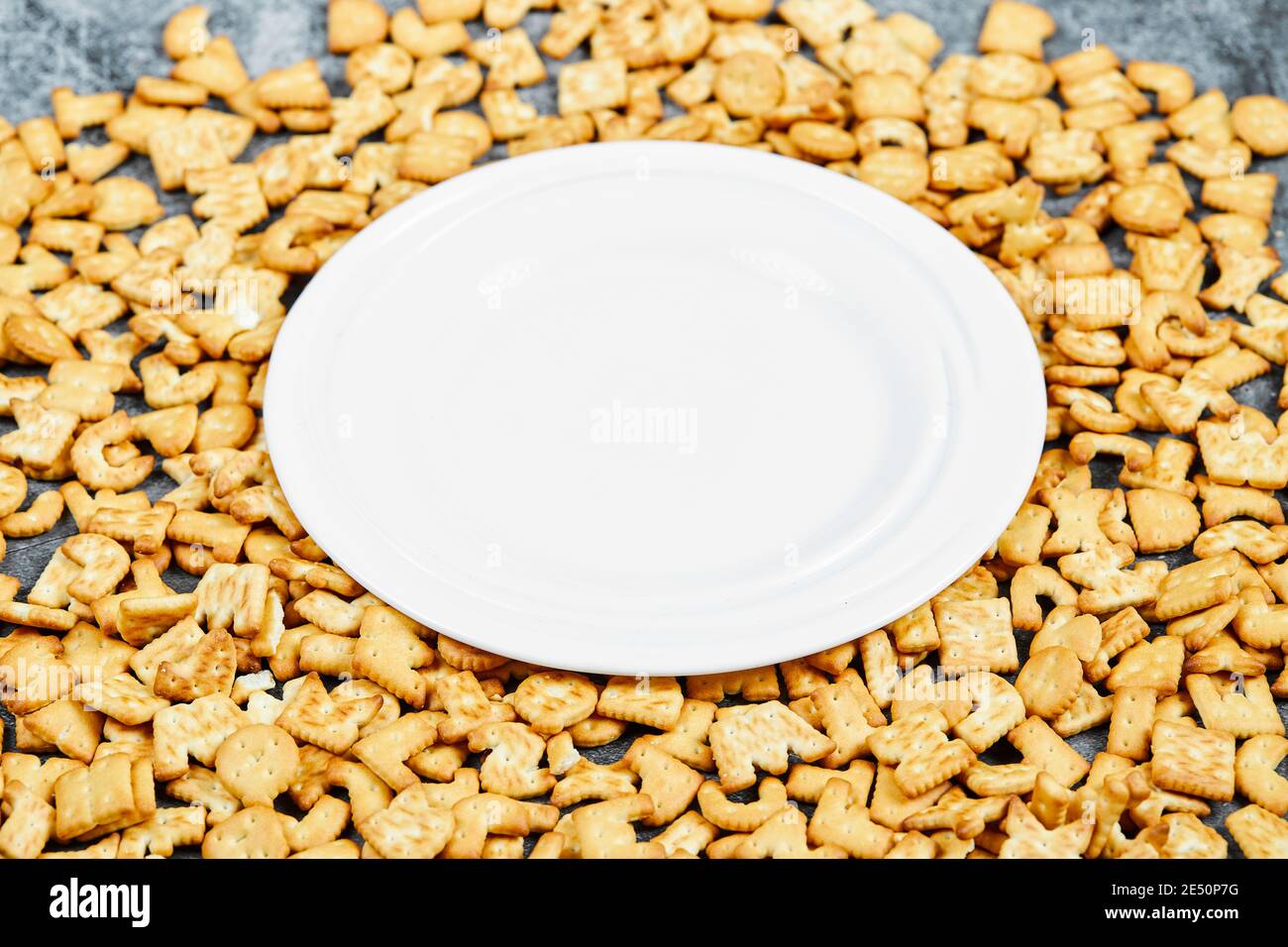 Scattered alphabet crackers around a empty plate on a marble background ...