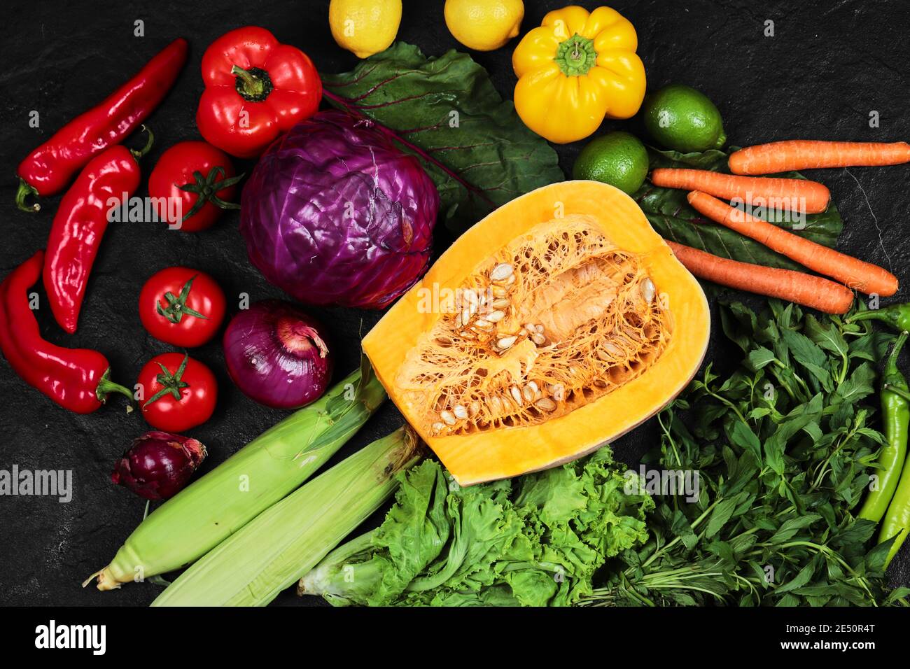 Half cut pumpkin and variety of fresh vegetables on black table Stock ...