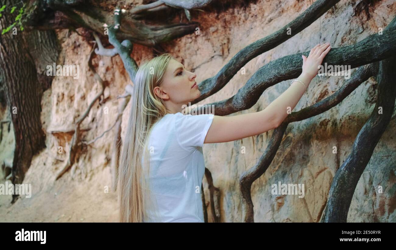 Young woman looking on exposed tree roots in natural loess ravine. Zoom ...