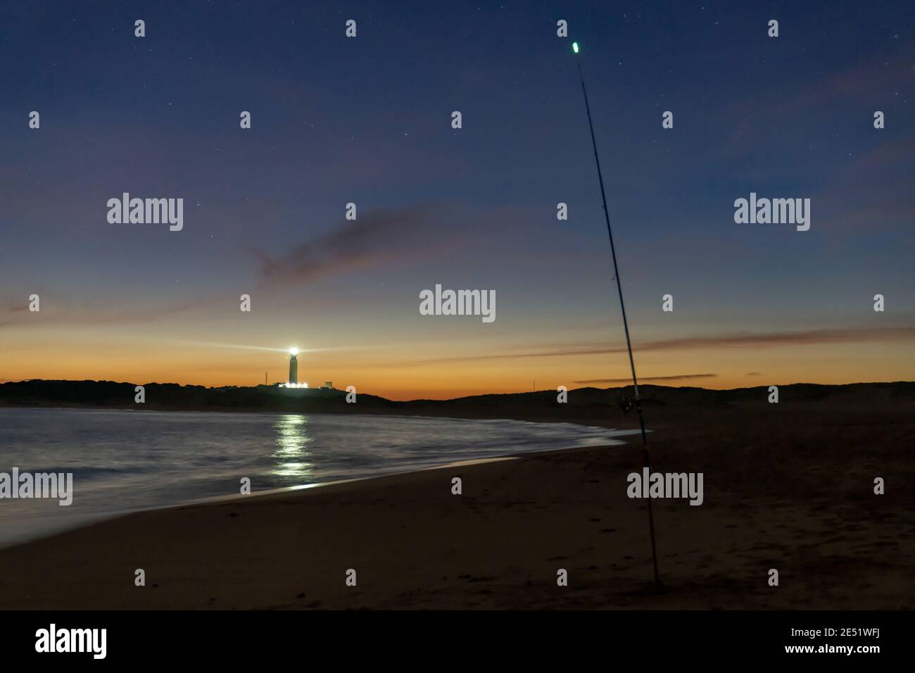 A fishing rod with luminescent tip on a beach at night with lighthouse ...