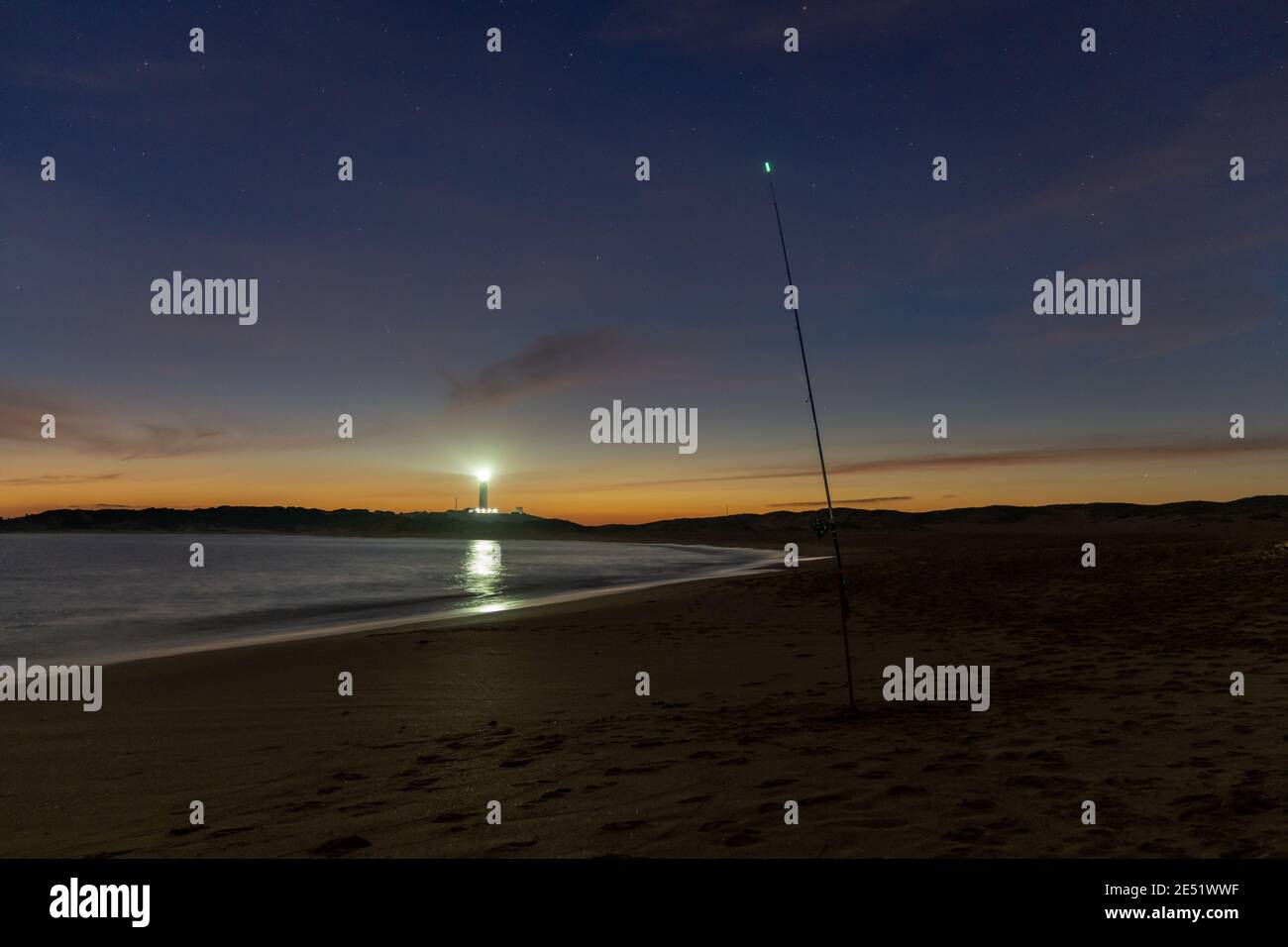 A fishing rod with luminescent tip on a beach at night with lighthouse ...