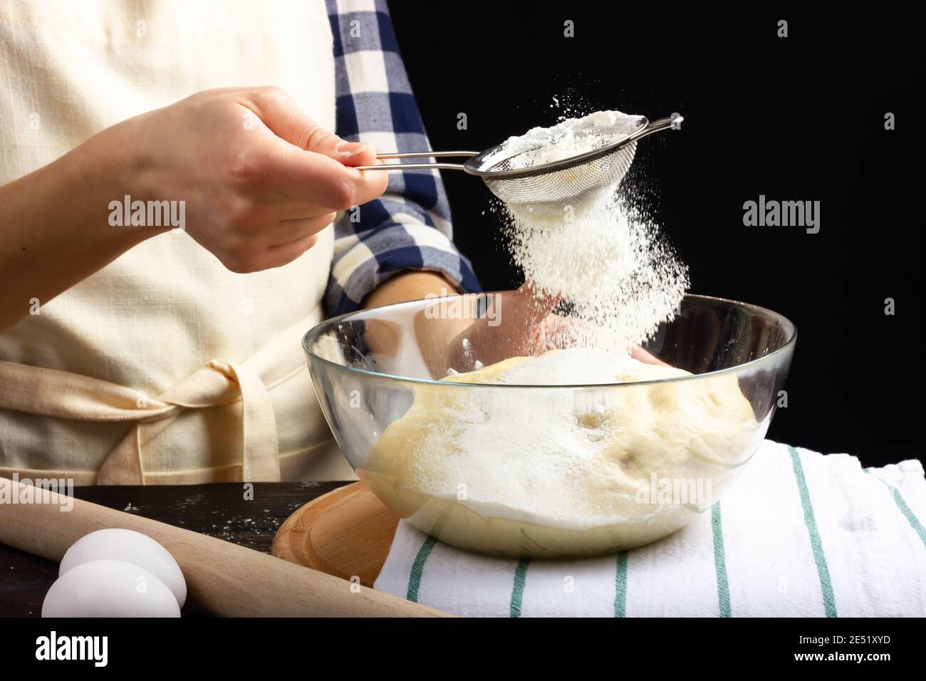 The woman is sifting flour into the dough. Sifting flour with a sieve ...