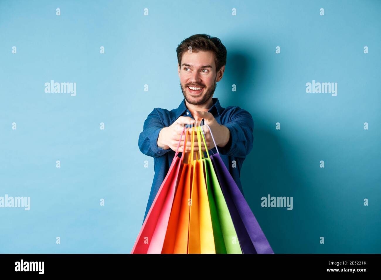 Handsome happy guy smiling, stretch out hands with shopping bags and ...