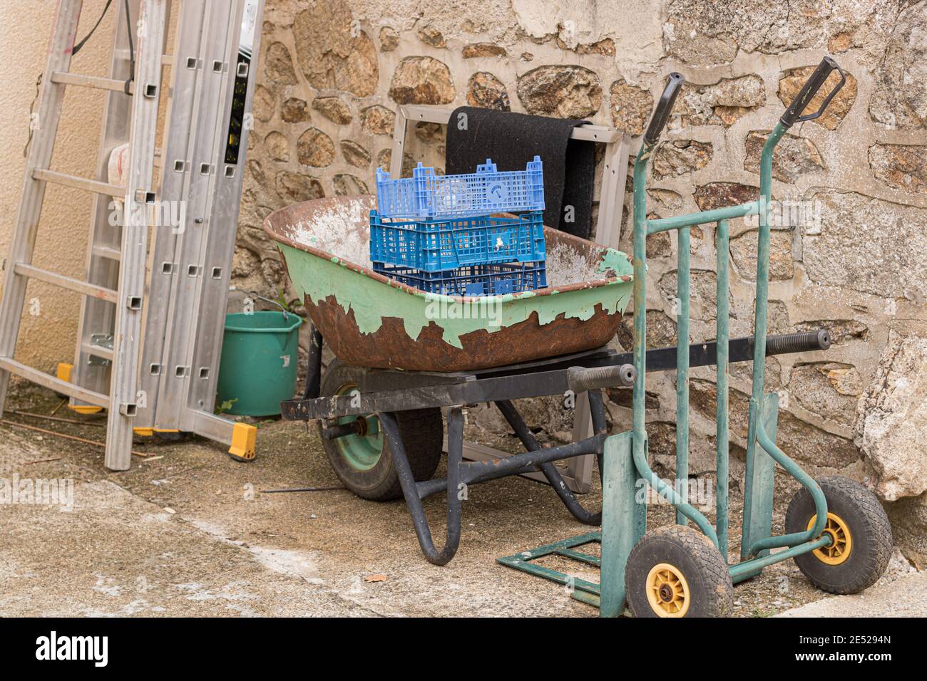Closeup shot of an old rusty wheelbarrow with boxes among other garden ...