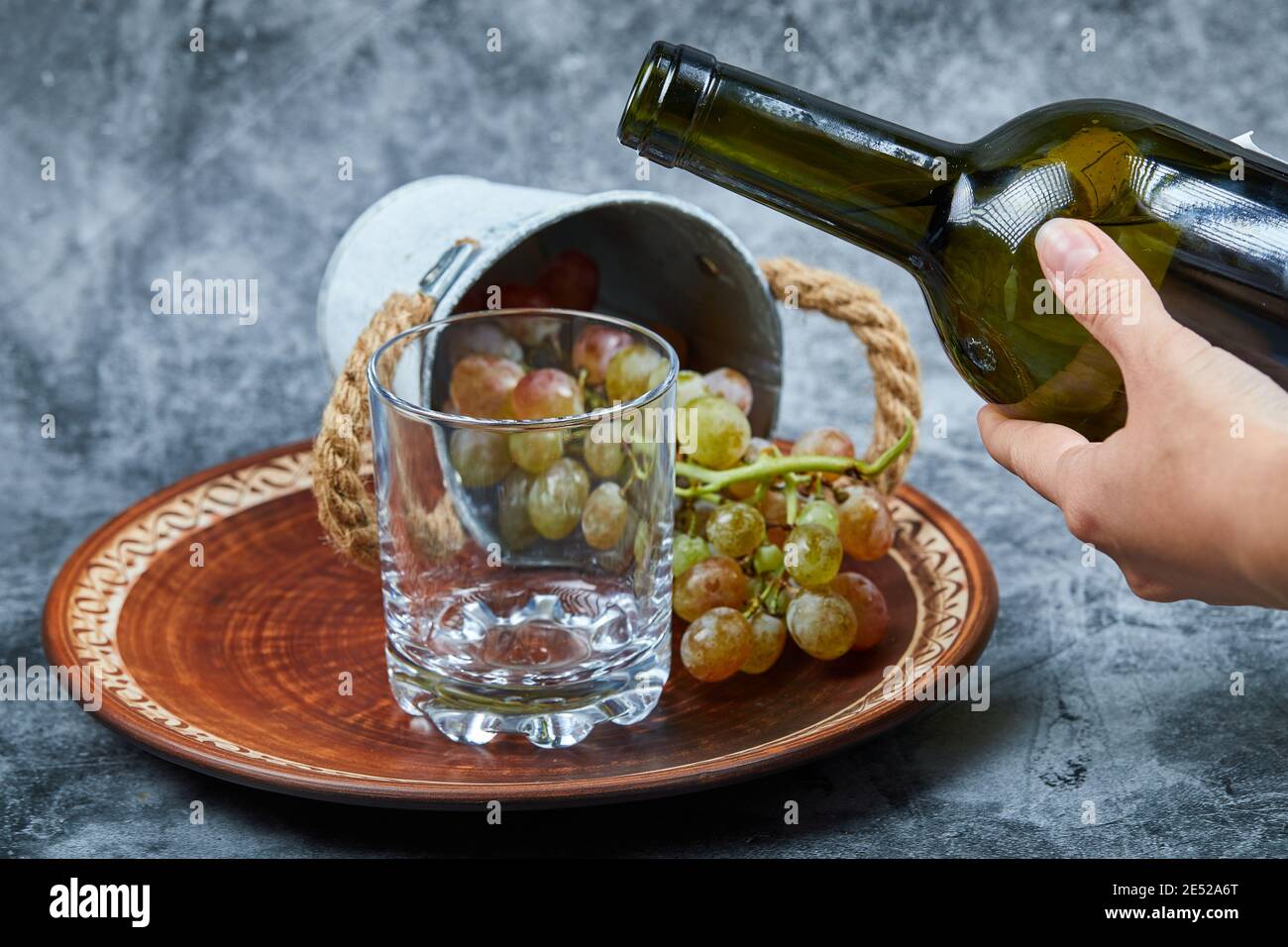 Small bucket of grapes inside ceramic plate and hand pouring wine into ...