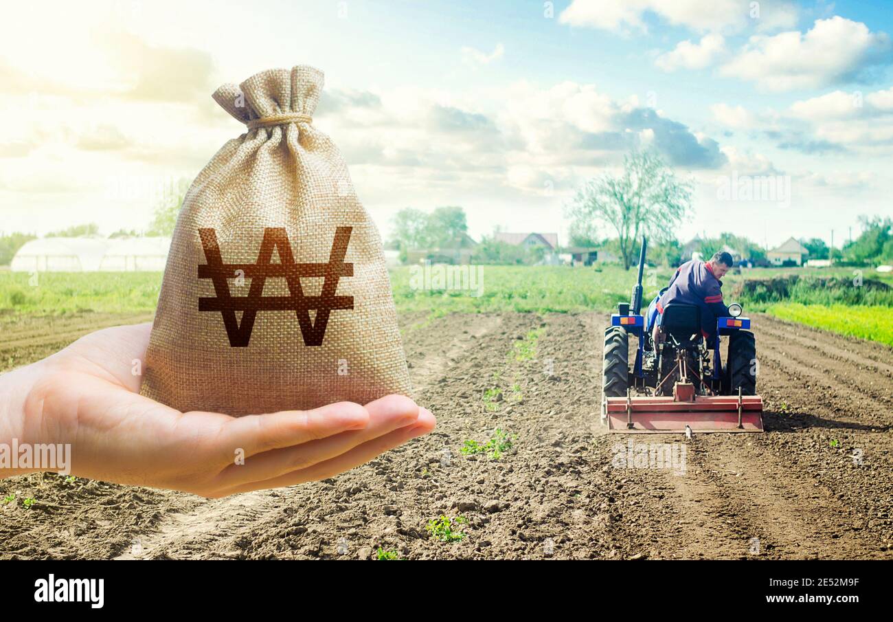 Hand with south korean won and a farmer on a tractor works on farm ...
