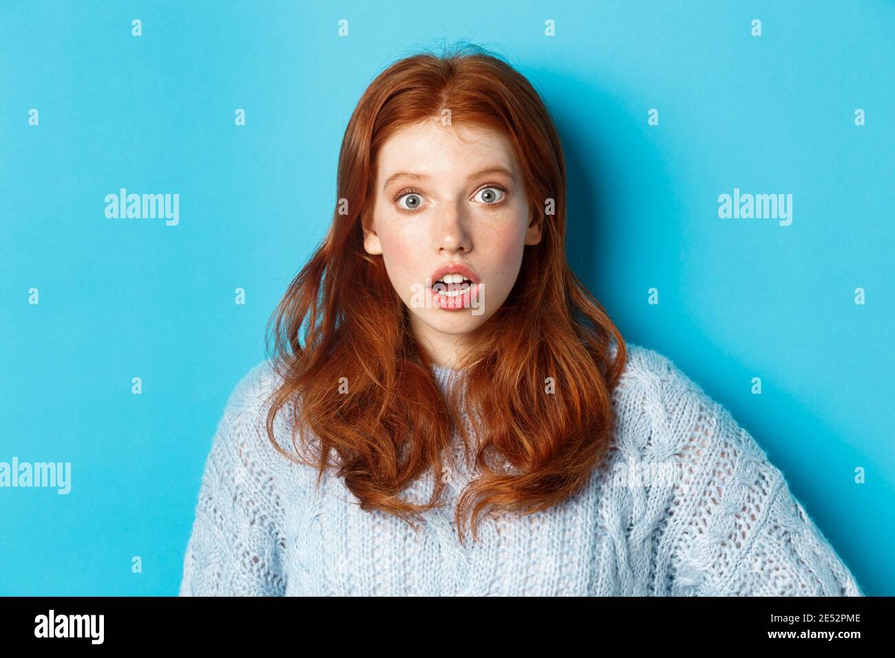 Close-up of startled redhead girl stare at camera speechless, open ...
