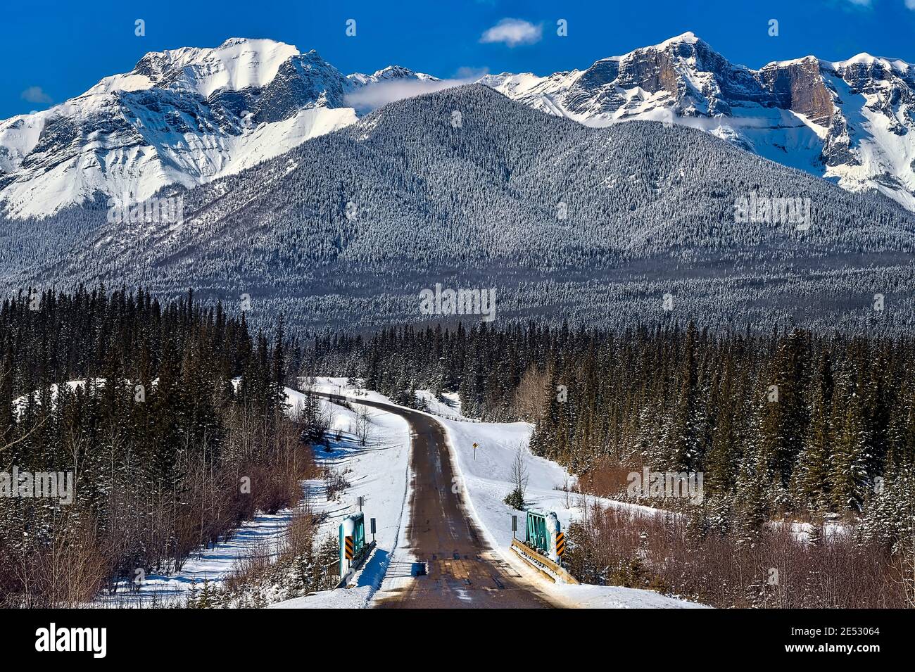 A two lane highway leading to the snow-capped rocky mountains at the ...