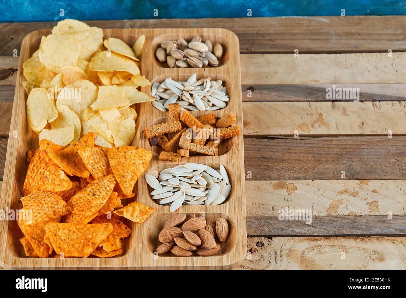 Plate of assorted snacks on a wooden table. Chips, crackers, almonds ...