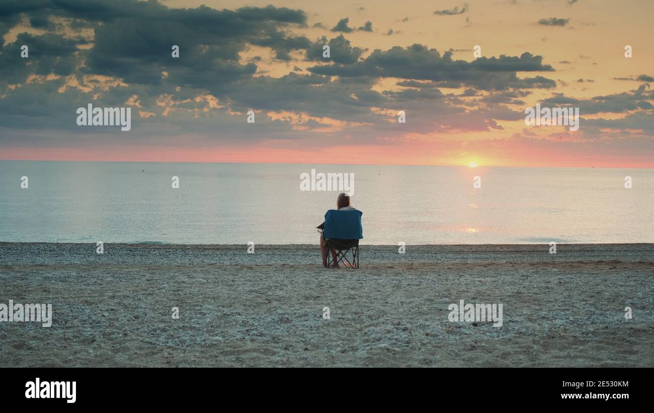 Back view of woman admiring sunset on the sea sitting in folding ...