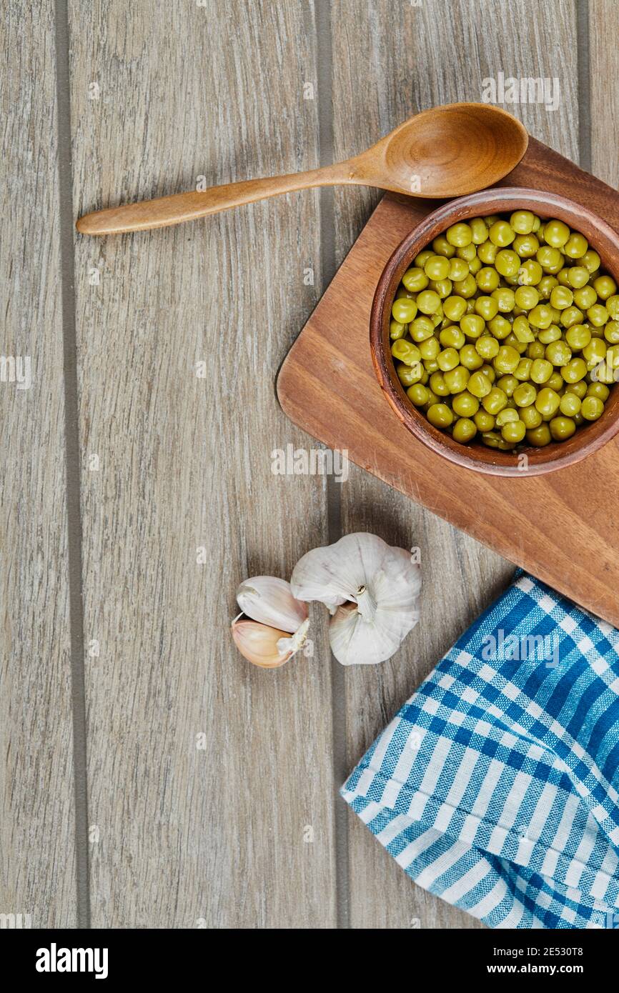 A bowl of boiled green peas with a spoon, garlic, and a blue tablecloth ...