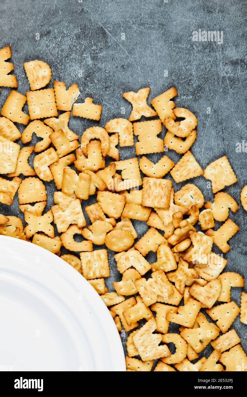 Scattered alphabet crackers around a empty plate on a marble background ...