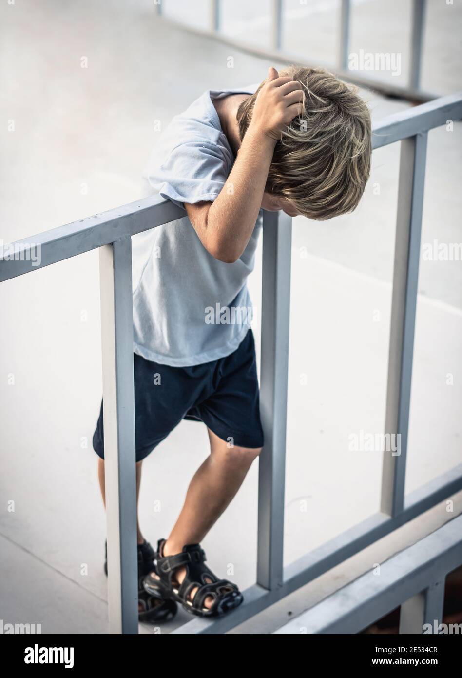 VERTICAL Little kid boy stand near bridge edge fence, look down touch ...