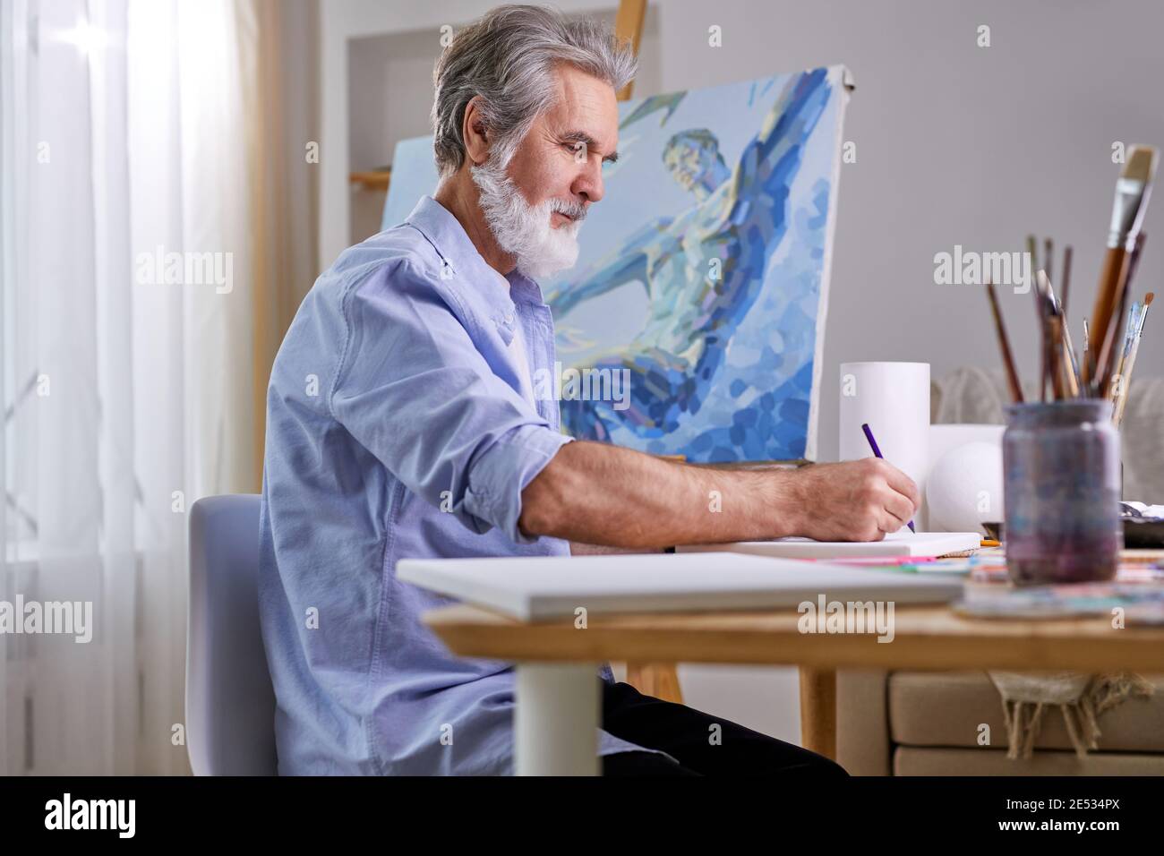 painter is drawing at home in light room, gray bearded man is creating ...