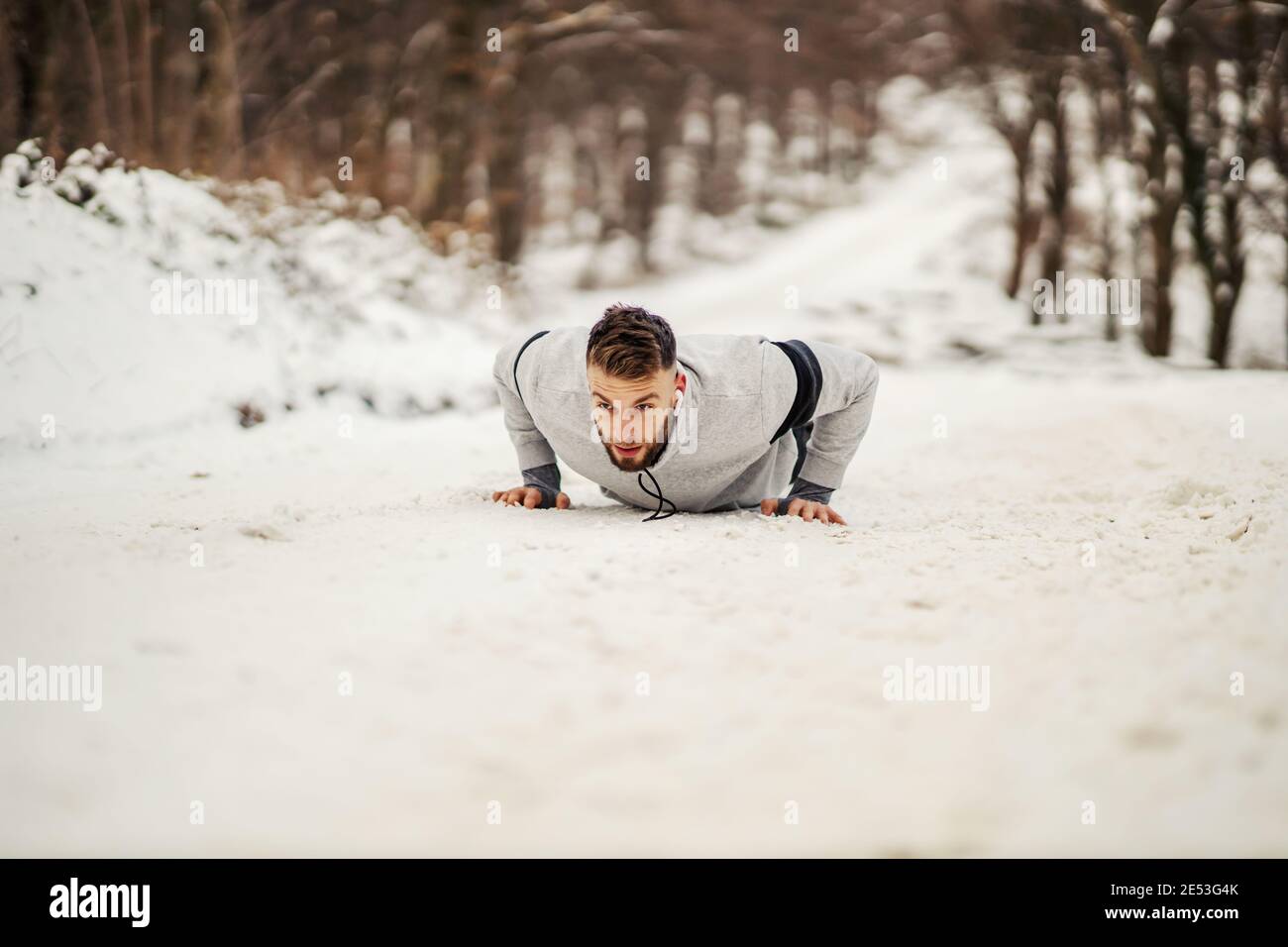 Strong sportsman doing push ups in nature on snowy path at winter ...