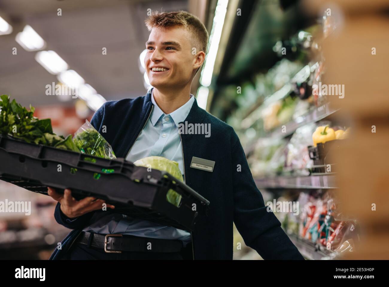 Male worker stocking up the vegetable section in supermarket. Man ...