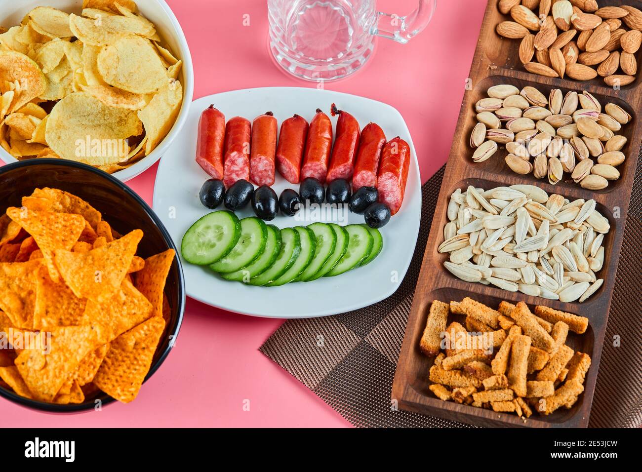 Assorted snacks on the pink table. Chips, sausages, pistachios, olives ...