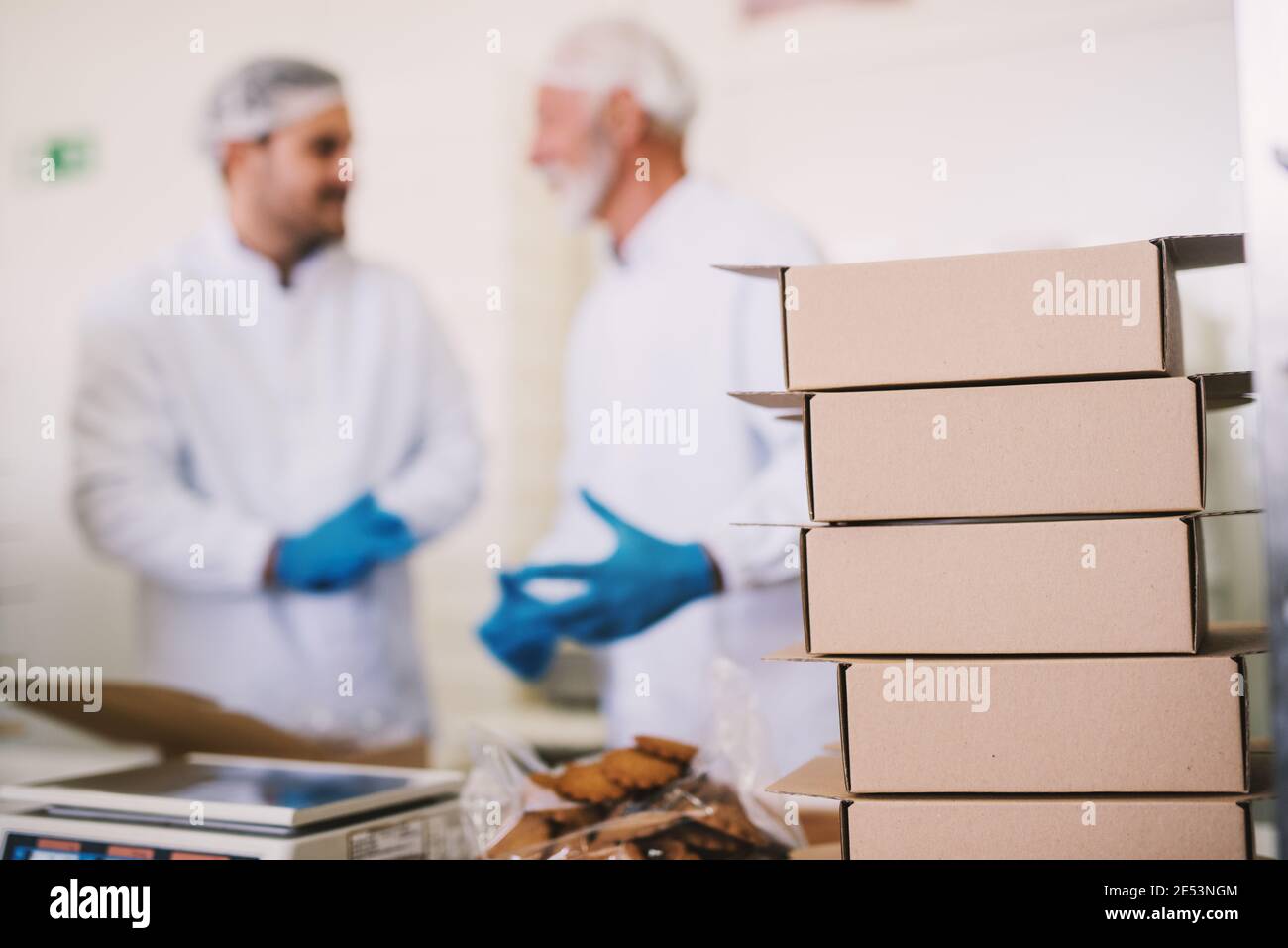 Picture of group of boxes in food factory. Blurred picture of two man ...