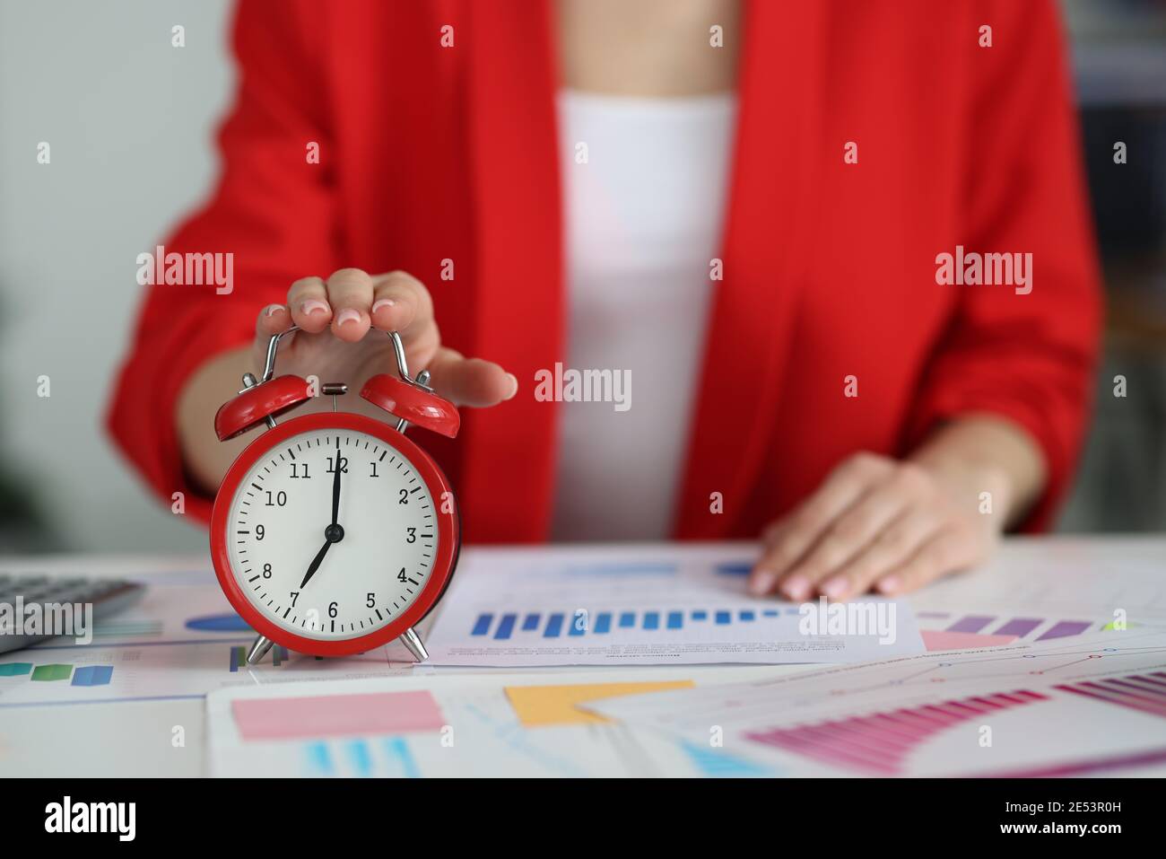 Woman in red jacket turning off alarm clock at table Stock Photo - Alamy
