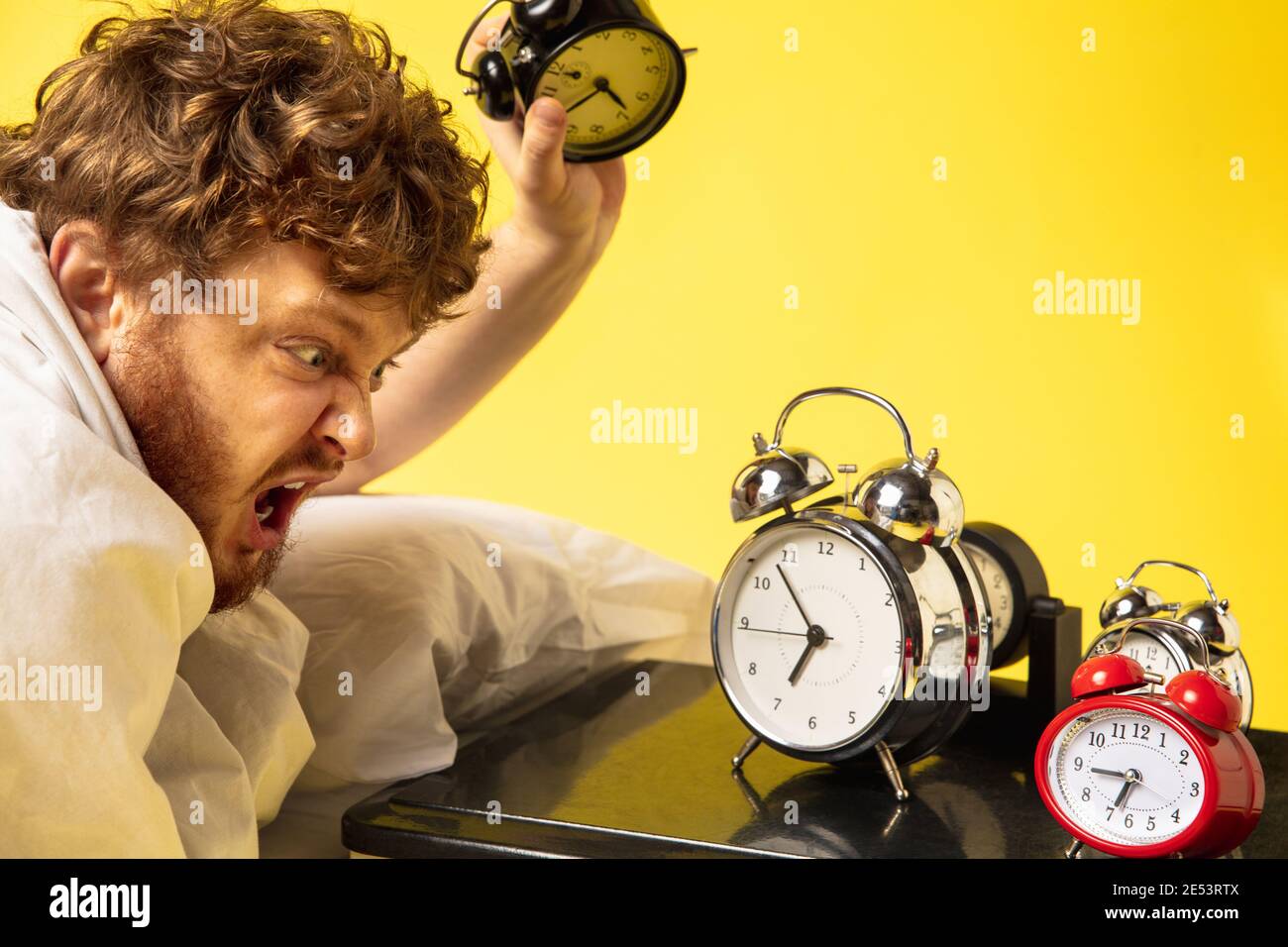 Man wakes up at his bed on yellow background and he's mad at clocks ...