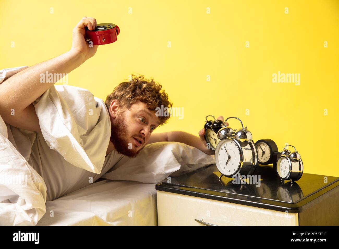 Man wakes up at his bed on yellow background and he's mad at clocks ...