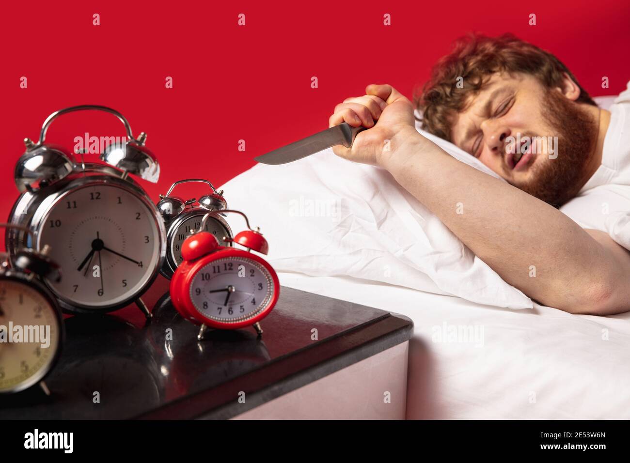 Man wakes up at his bed on red background and he's mad at clocks ...