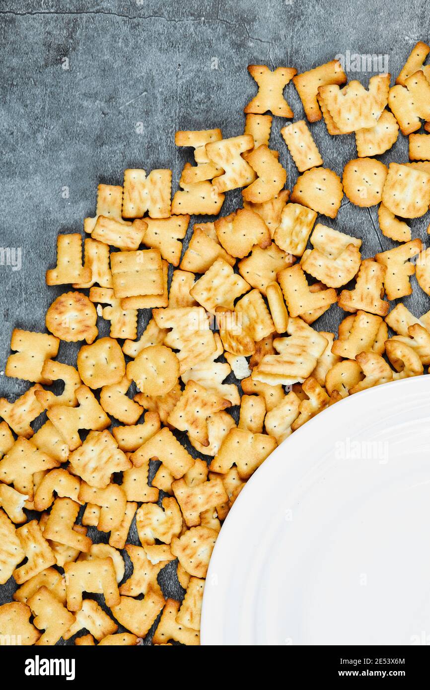 Scattered alphabet crackers around a empty plate on a marble background ...