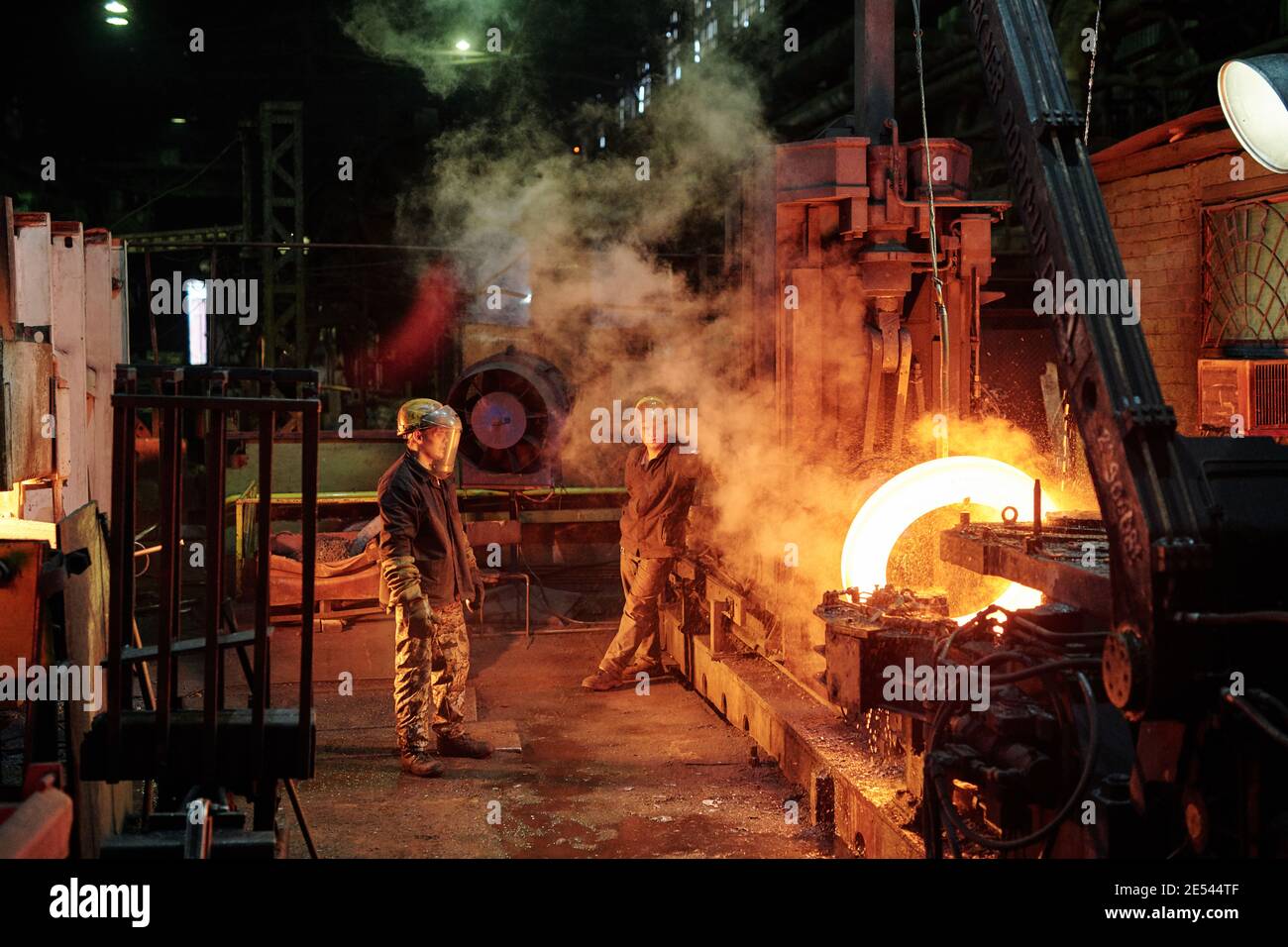 Group of workers in helmets melting metal in metal fabrication plant ...