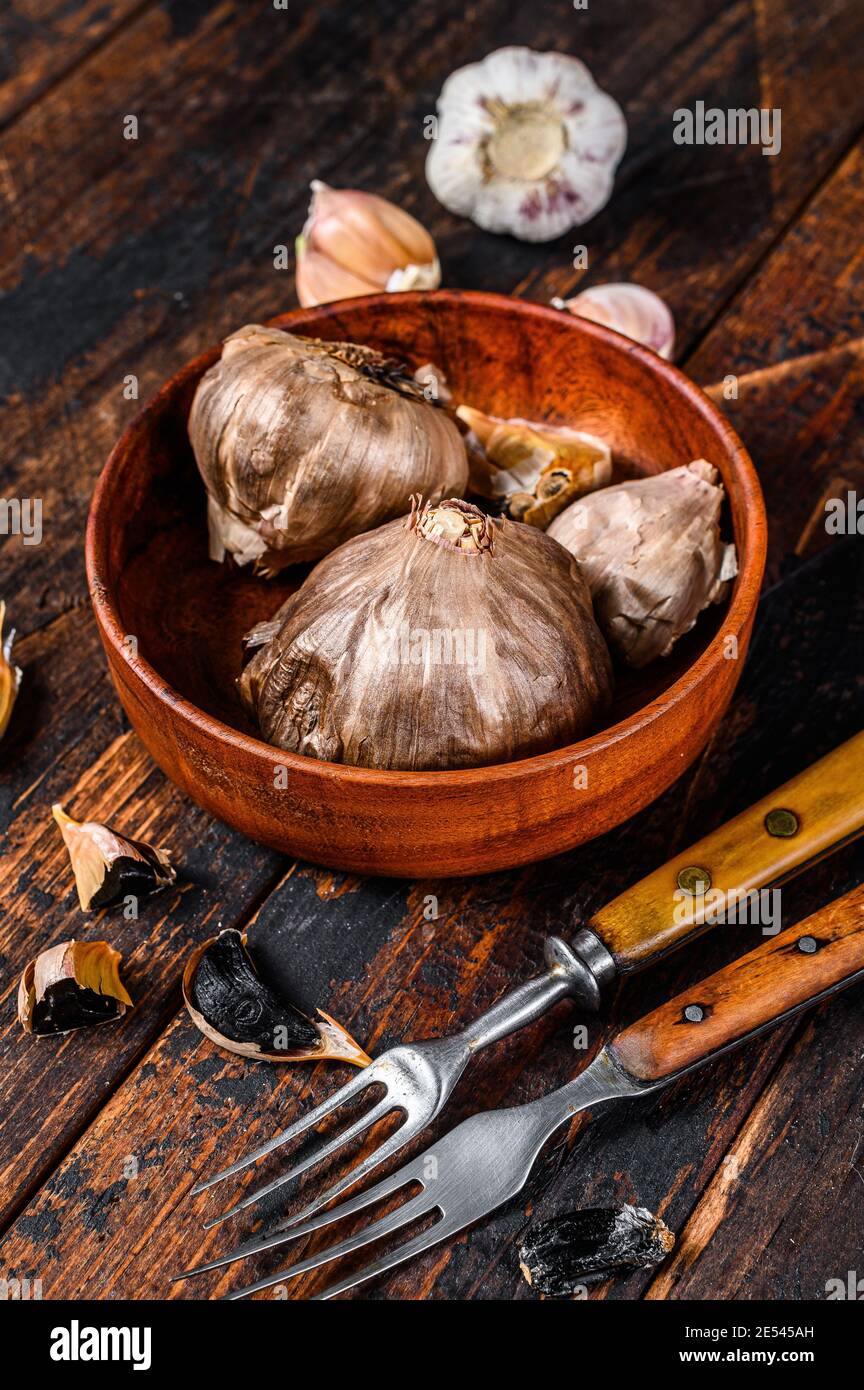 Bulbs and cloves of fermented black garlic in a plate. Dark wooden ...