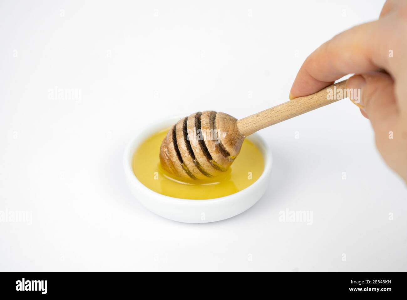 Liquid honey pouring with wooden stick in small white plate Stock Photo ...