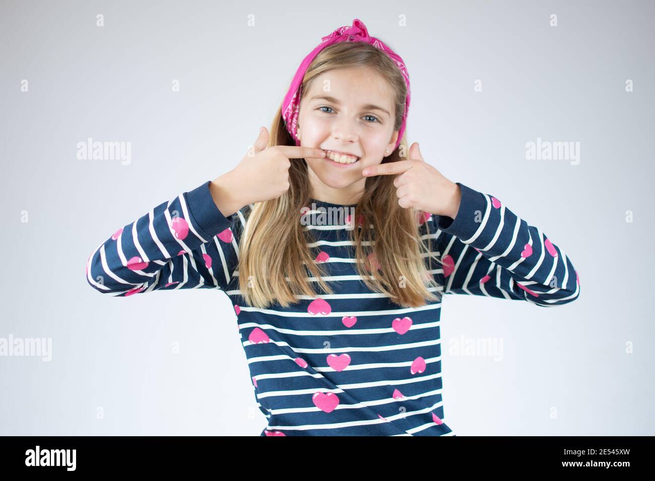 Cute little girl smiles pointing fingers at mouth over white background ...