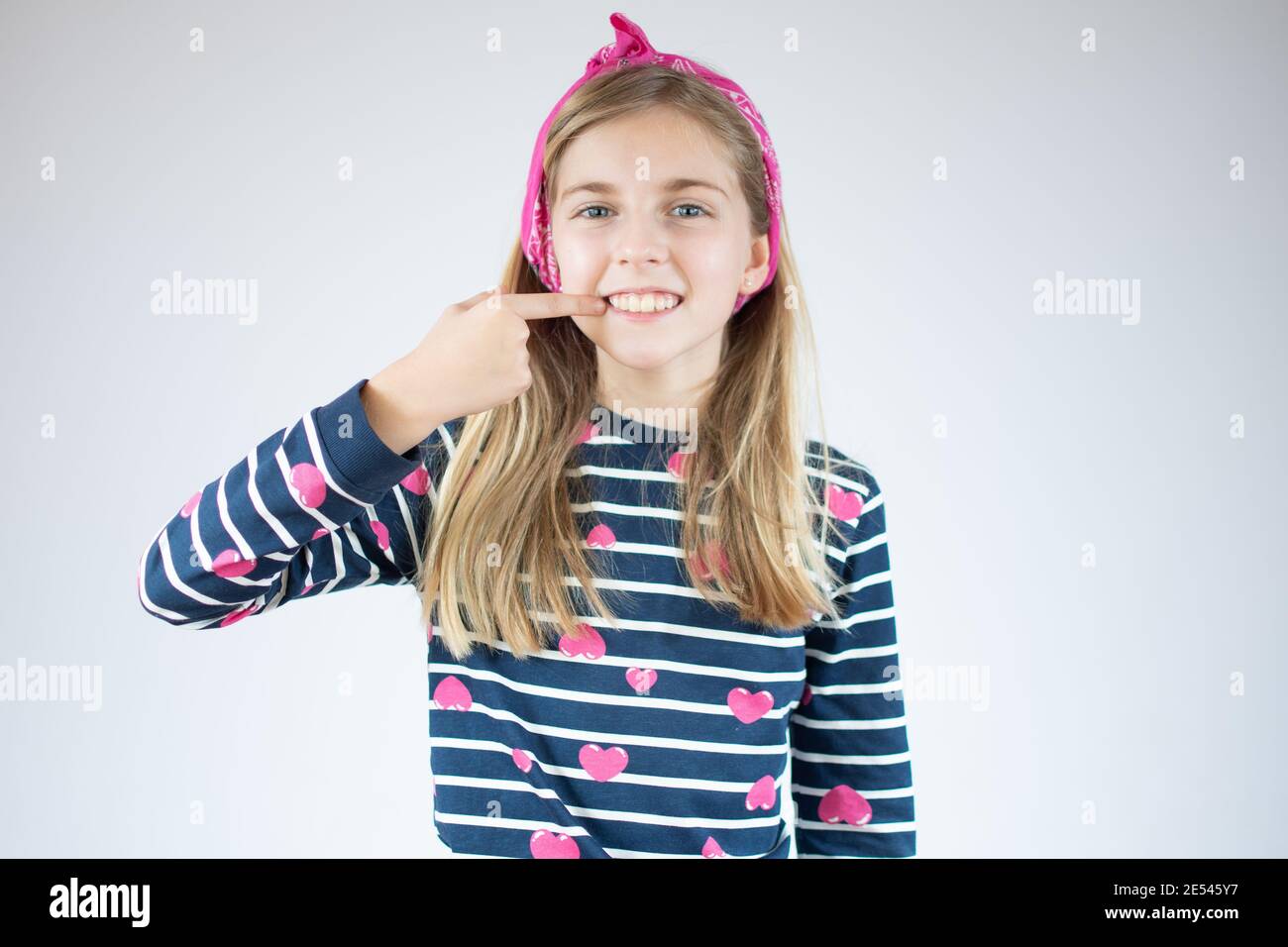 Cute little girl smiles pointing fingers at mouth over white background ...