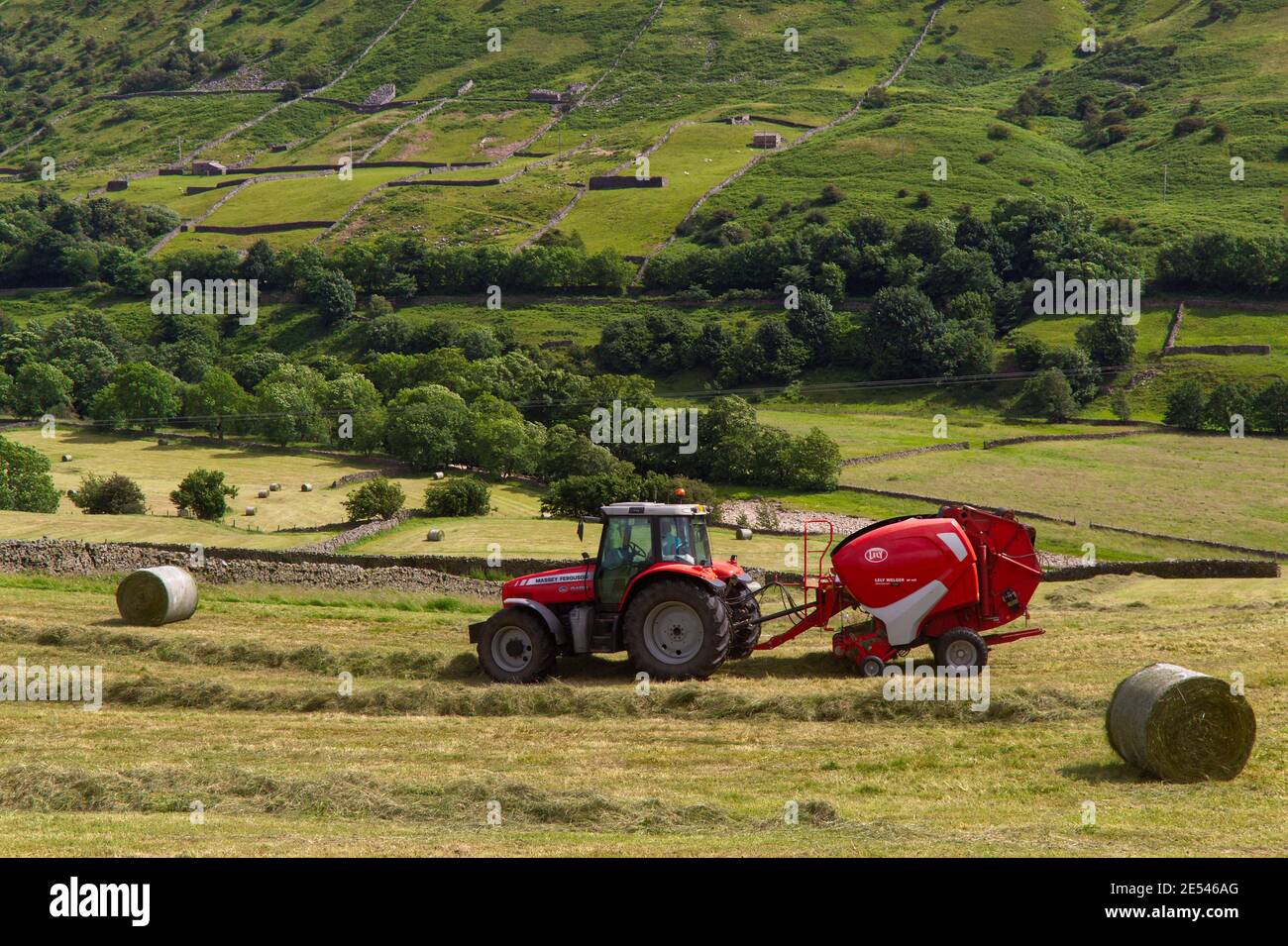 A farmer baling hay into large bales with a Massey Ferguson tractor ...
