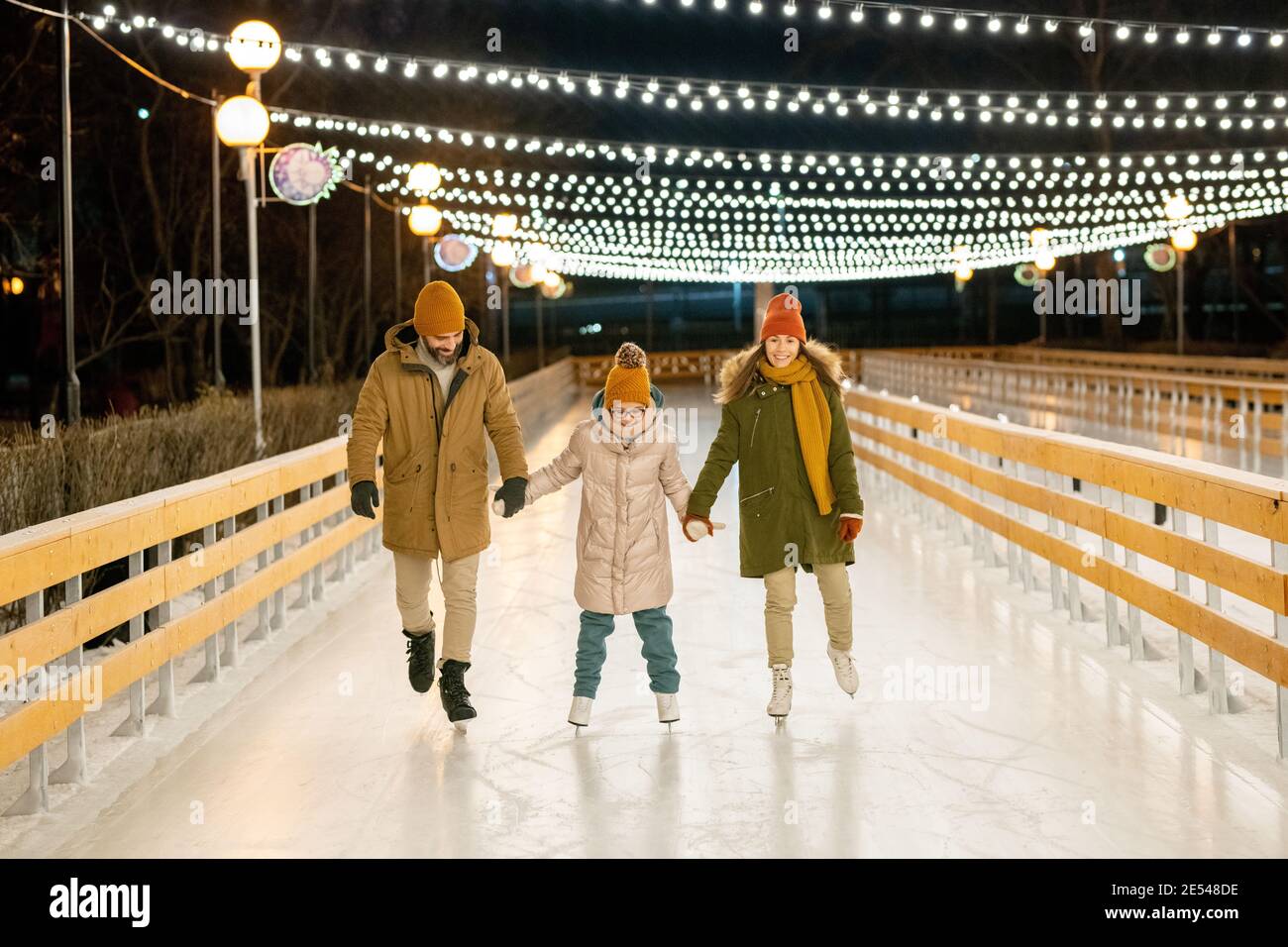 Two parents teaching their daughter to skate they holding hands and ...