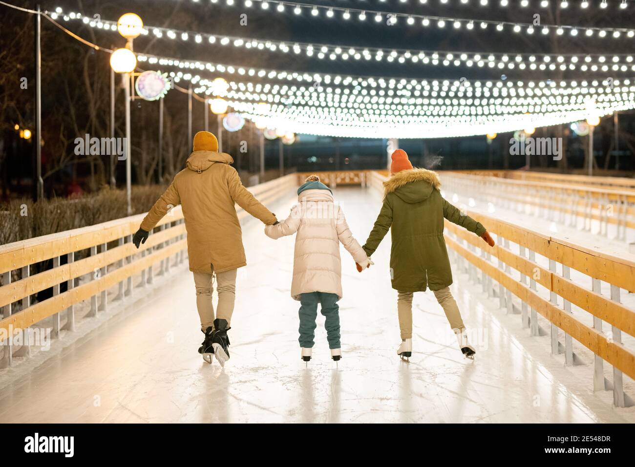 Rear view of family of three in skates holding hands and skating ...