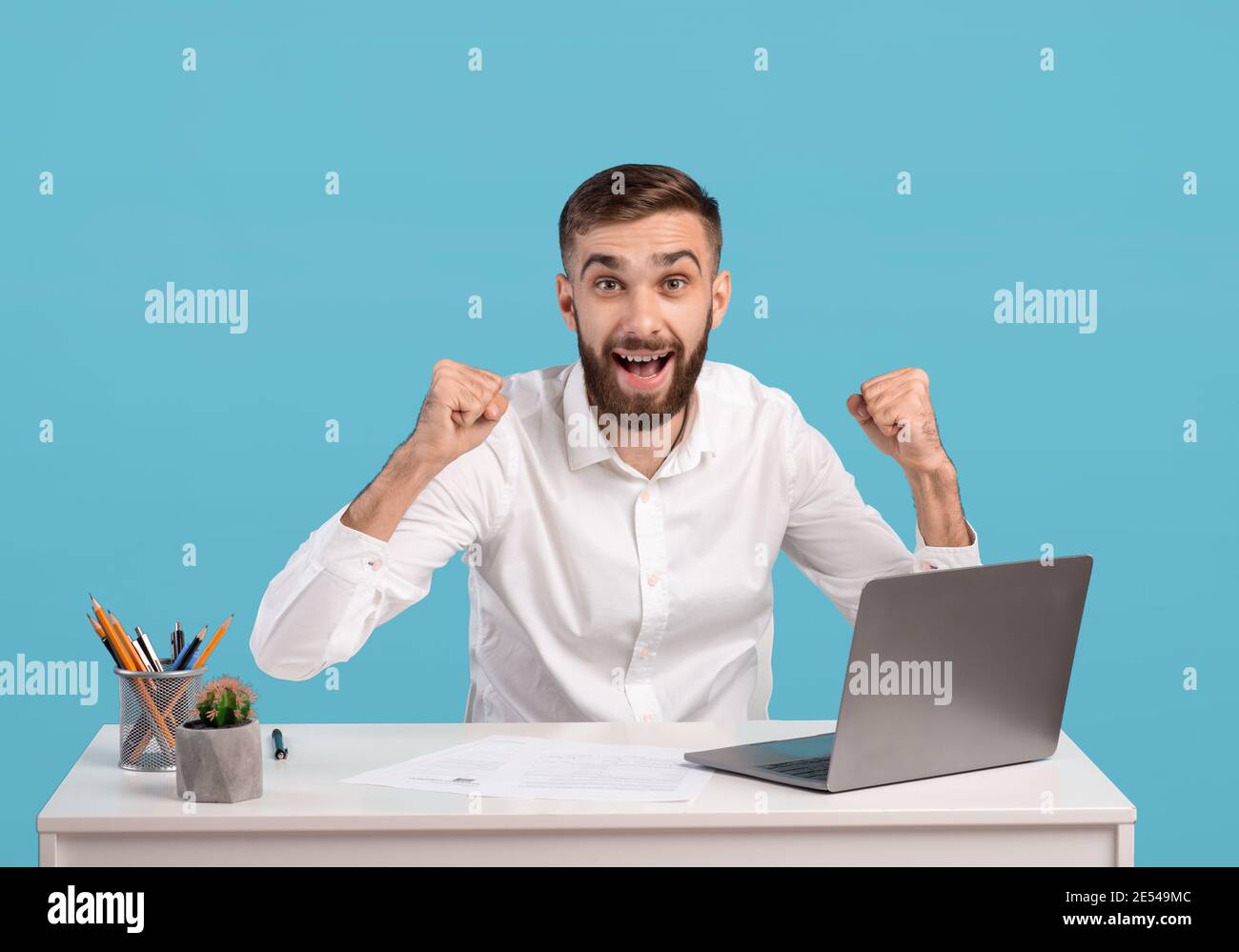 Positive young businessman making YES gesture while working on laptop ...