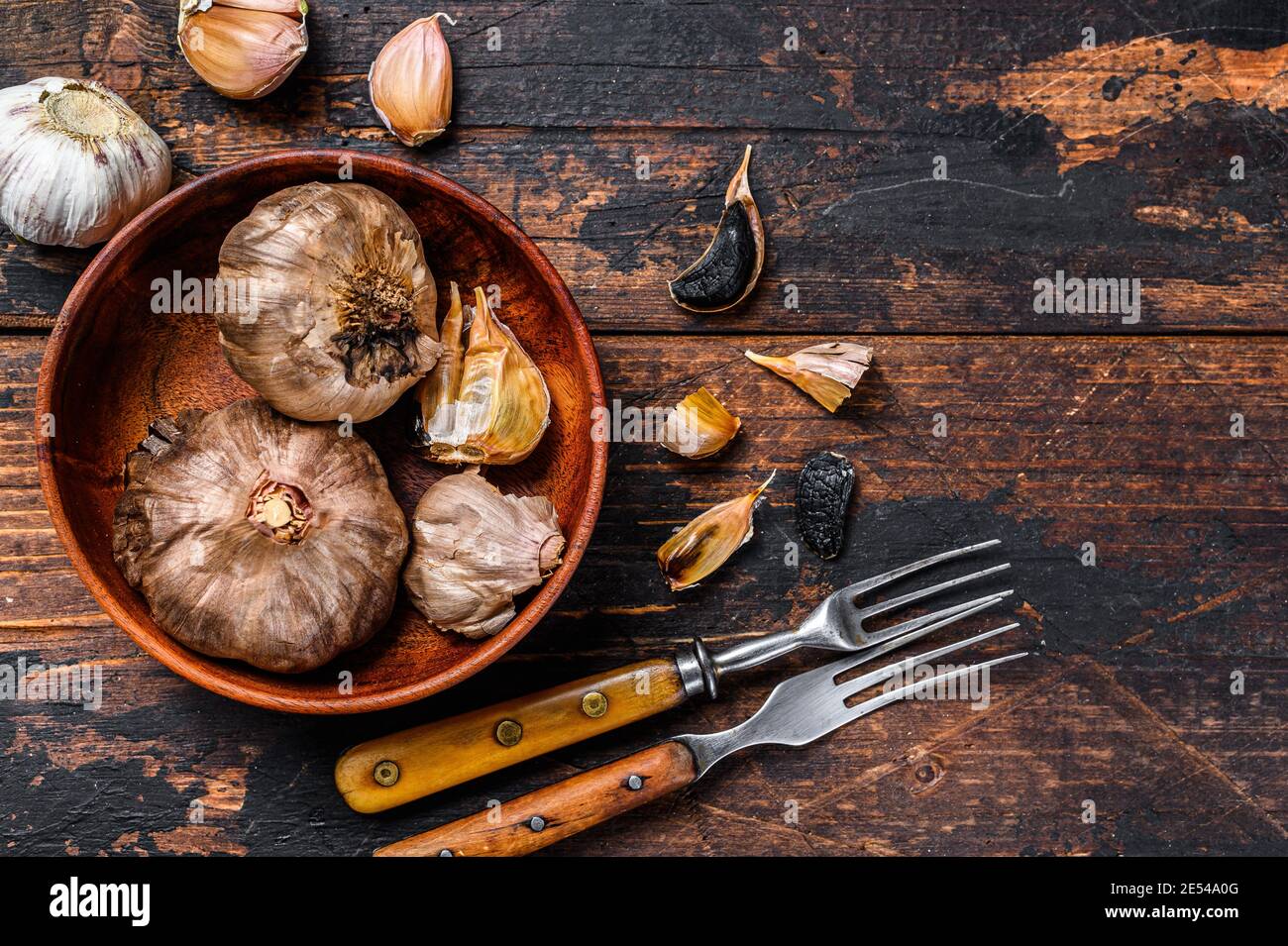 Bulbs and cloves of fermented black garlic in a plate. Dark wooden ...