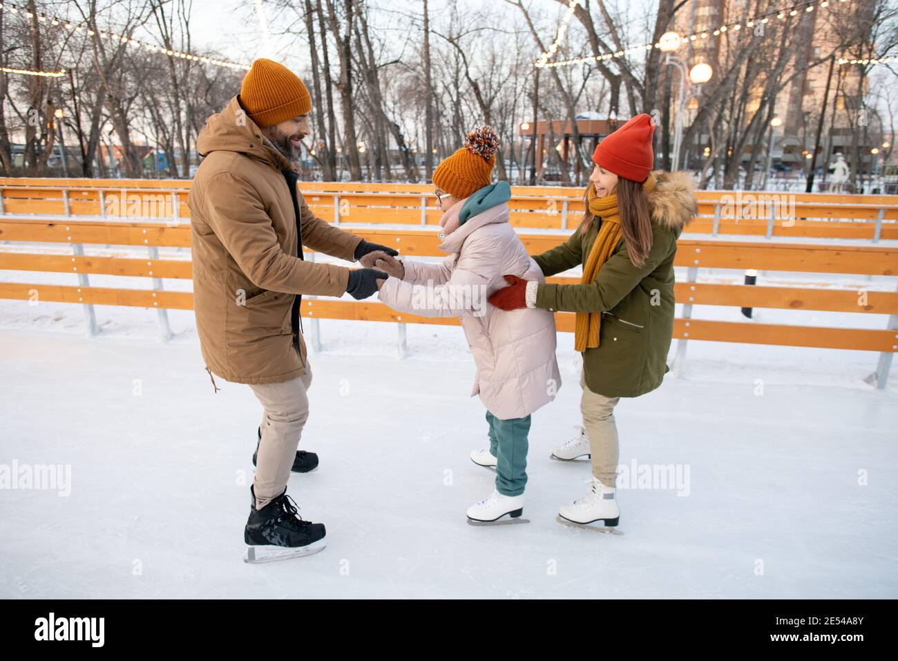 Parents teaching their child to skate on ice rink outdoors during ...