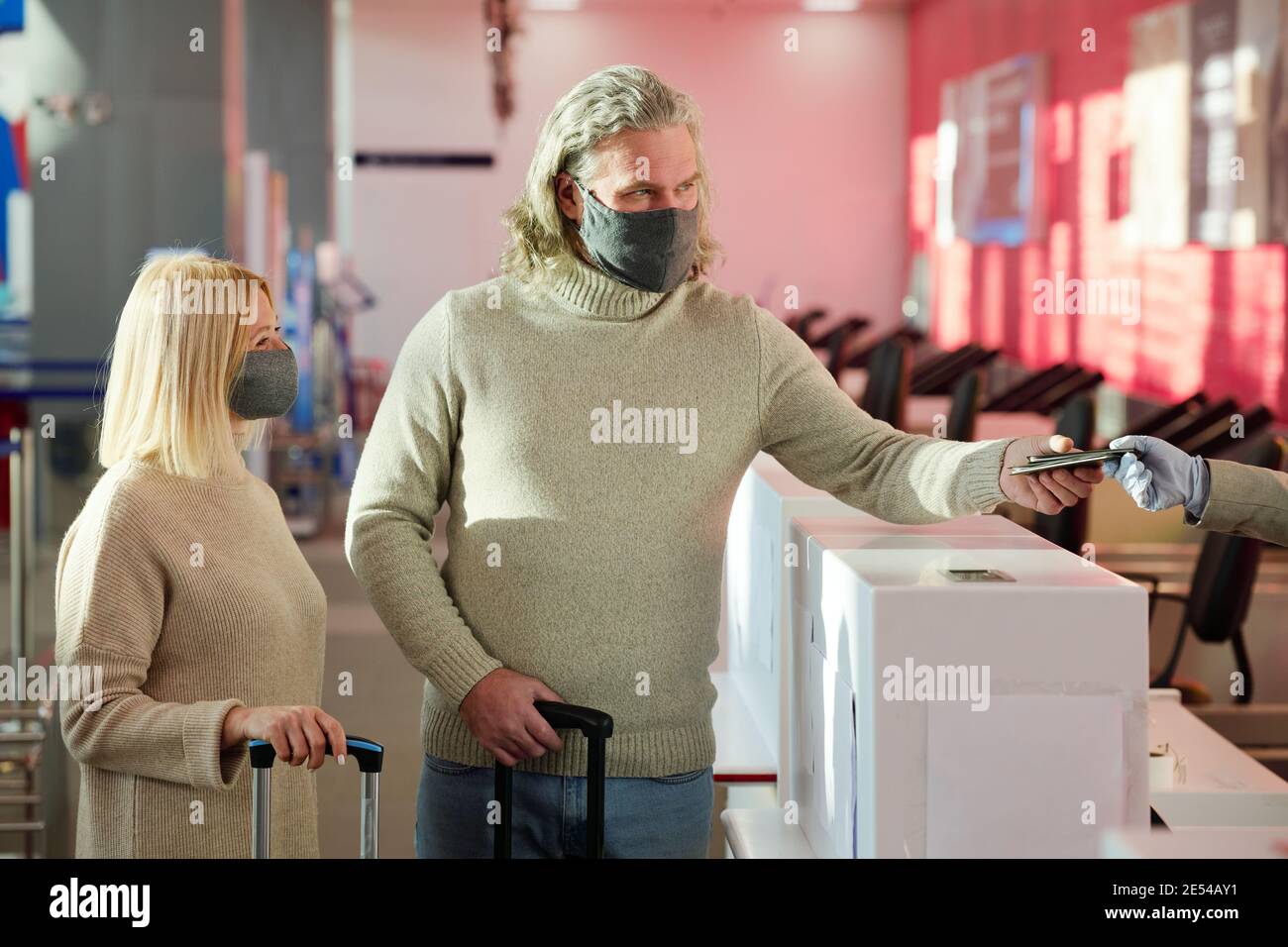 Young couple in protective masks standing with luggages at reception ...