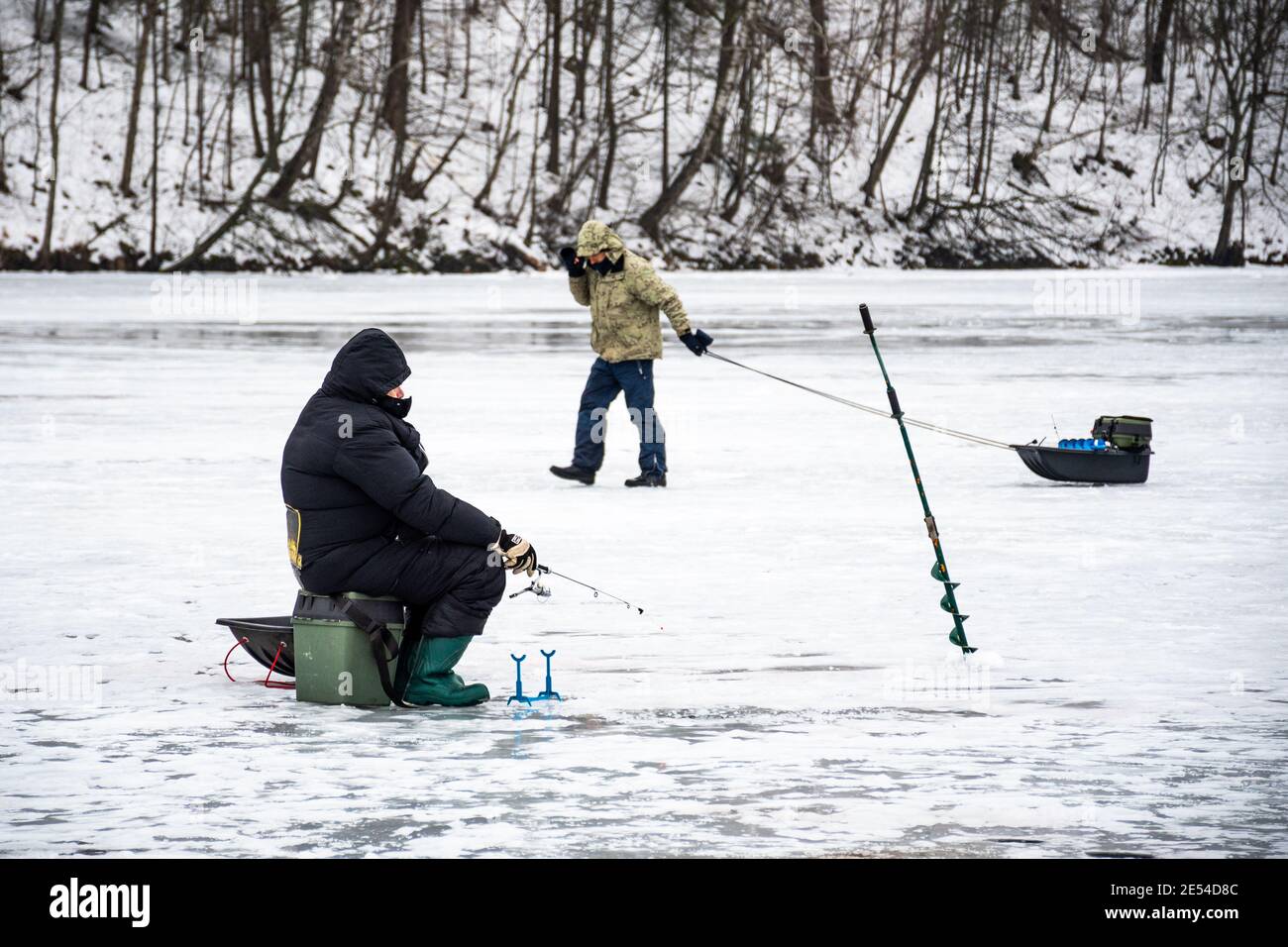 Fisherman fishing on a frozen lake in winter with fishing pole or rod ...