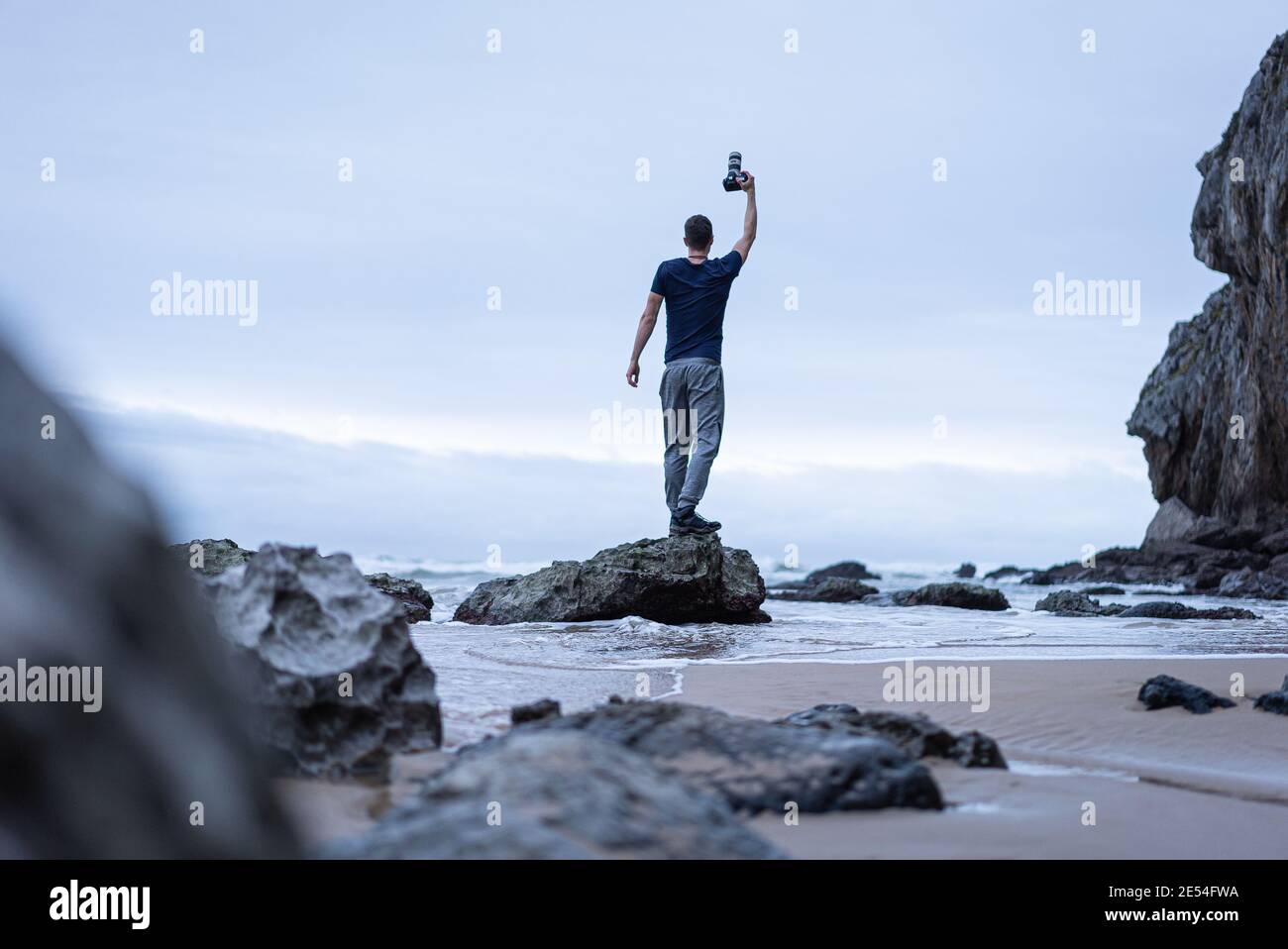 Cool male photographer holding camera standing on a stone in the ...