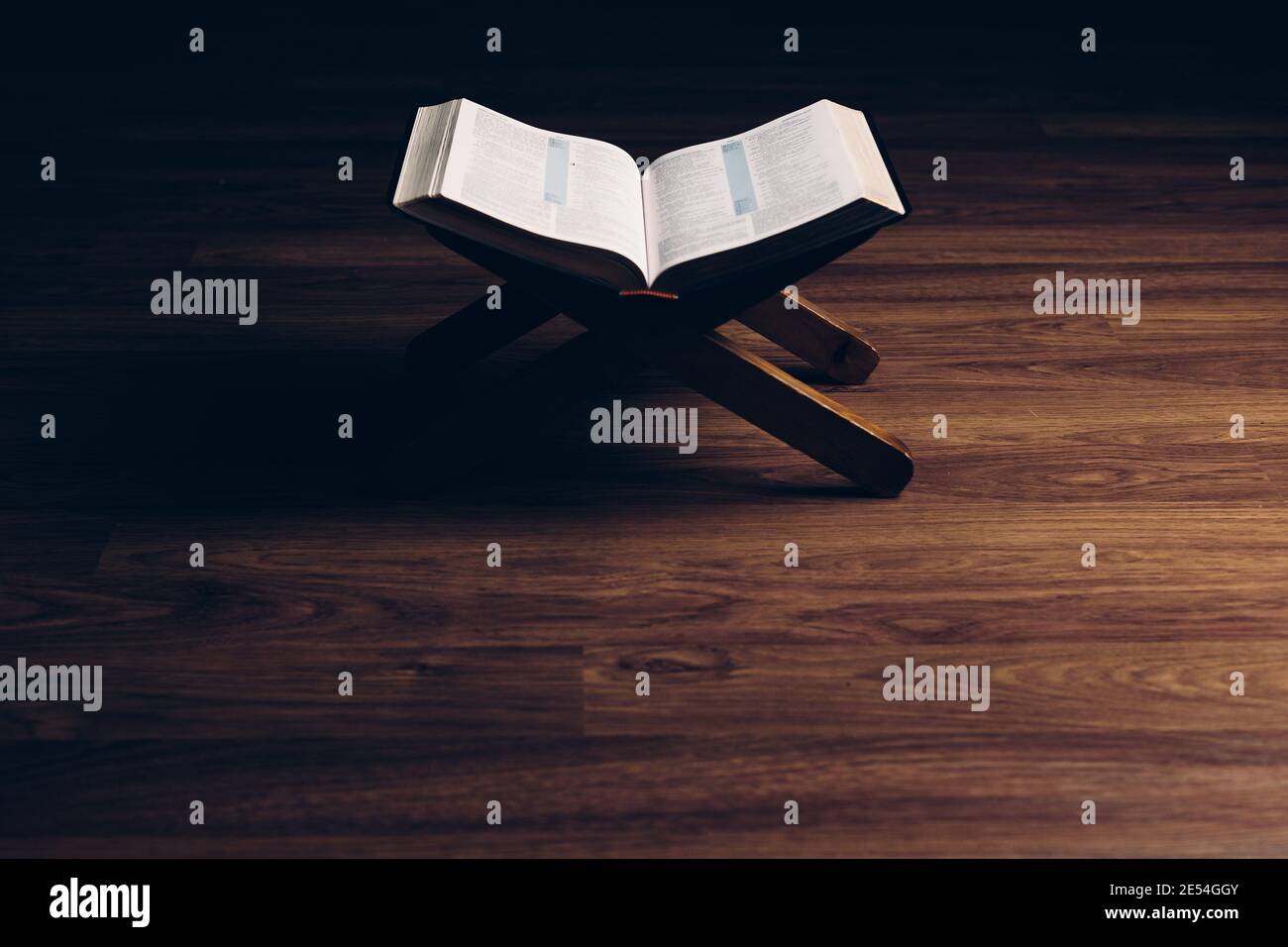 open bible on a book stand on a black background with a wooden floor ...