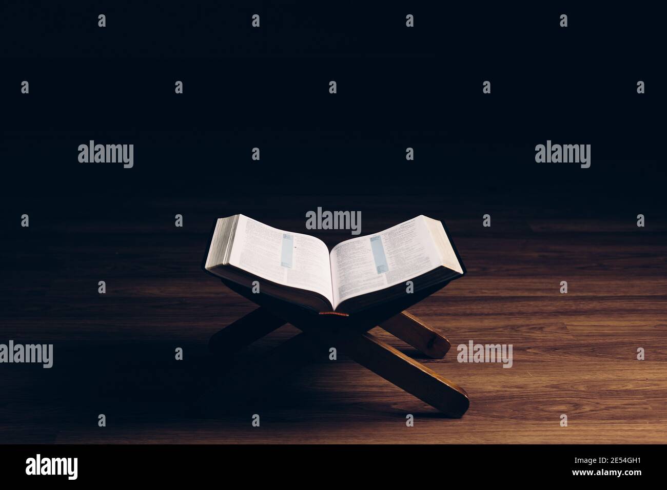 open bible on a book stand on a black background with a wooden floor ...